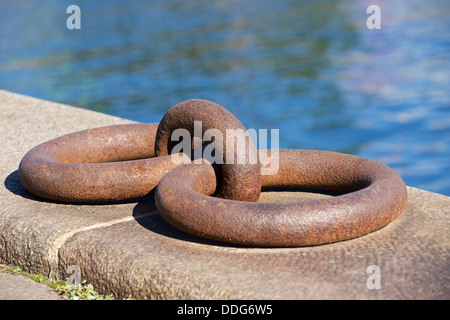 Rusty metal dock ring with mooring rope tied at marina pier near calm ...