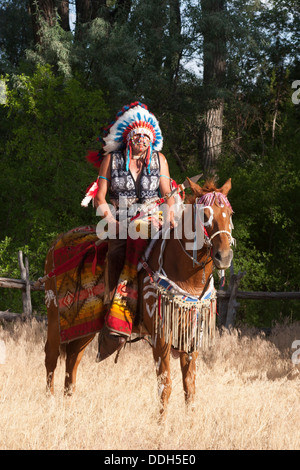 Warrior in Comanche clothing riding chestnut horse decorated in war ...