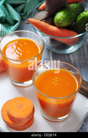 glasses of carrot juice and fresh carrots on wooden table on green ...