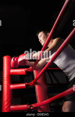 Serious male boxer resting his elbows on the ring side, looking away ...