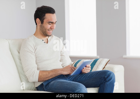 Happy young man using tablet computer while sitting on sofa at home ...