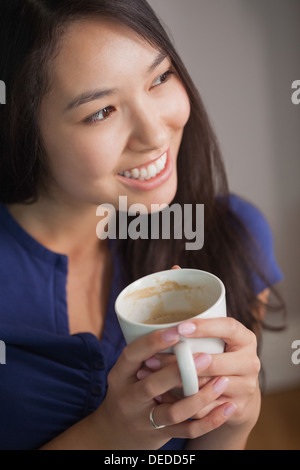 Asian woman holding coffee mug smiling at laptop computer working from ...