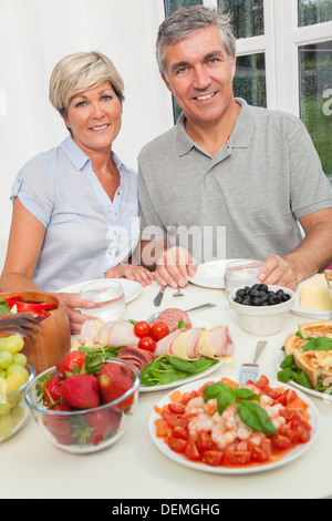 Middle-aged man smiling while eating fresh vegetable salad at home ...