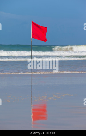 A red Safety flag flapping in the wind with large waves breaking on the ...