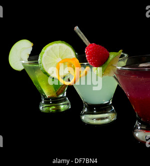 three bright martinis garnished with fresh fruit isolated on a black ...