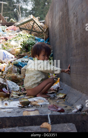 A young girl is defecating in a dumpster filled with garbage on a trash ...