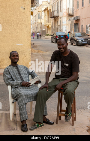 Two senegalese men in traditional clothing are sitting on a prayer rug ...