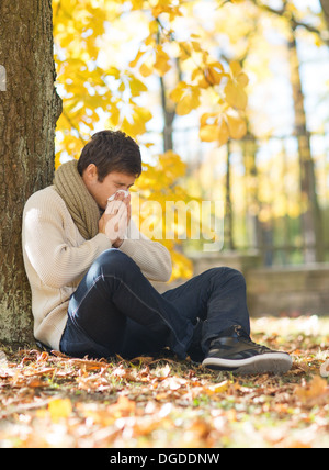 ill man with paper tissue in autumn park Stock Photo - Alamy