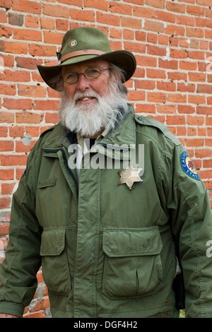 Old park ranger is standing outside on a stone patio holding a stick in ...