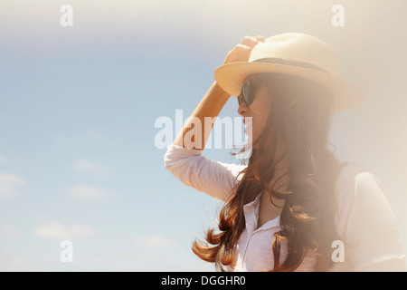 Young woman in white sunhat, sunglasses, and blue sundress. She is ...