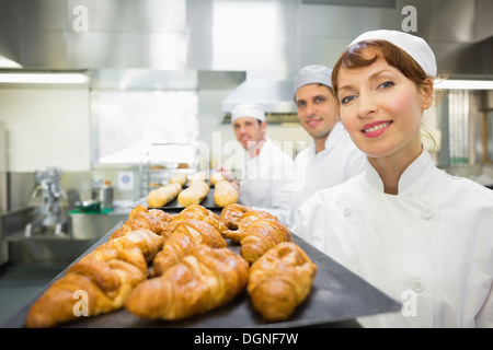 Three young bakers in uniform forming dough for baking on the wooden ...