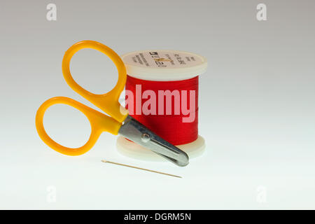 A spool of red thread, scissors, thread needle and thread shaped like a ...