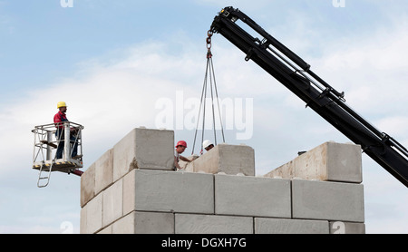 Workers place concrete blocks in row on building site surrounded by ...