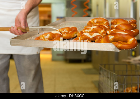 baker standing in his bakery in the morning and is baking bread or buns ...