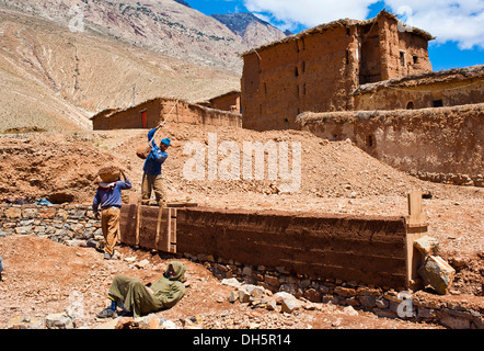 Worker building a rammed-earth wall for a new house, the clay is ...