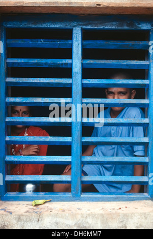 A boy looking through the barred window of a traditional Batak house ...