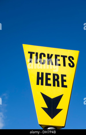 A yellow 'tickets here' sign with an arrow pointing downwards, against ...