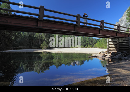Wooden footbridge over the Merced River in Yosemite Park. In the still ...