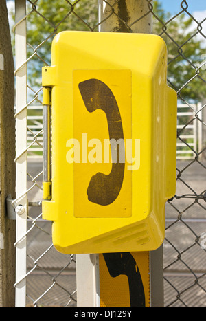 Yellow railway telephone box against wire mesh chainlink type fence ...