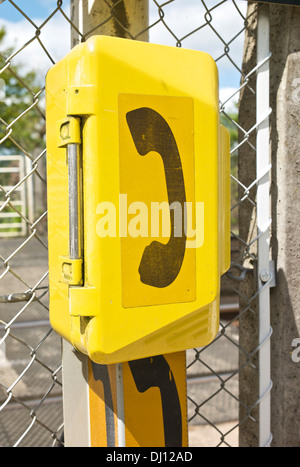 Yellow railway telephone box against wire mesh chainlink type fence ...
