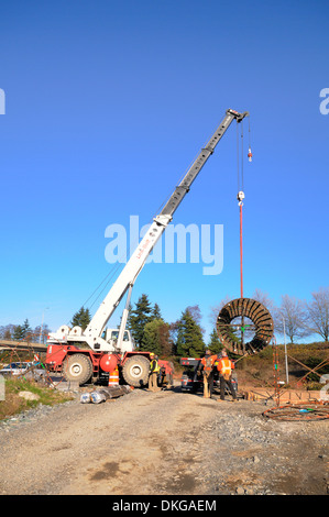 Workers offload rebar cylinder shape off flatbed truck, using a crane ...