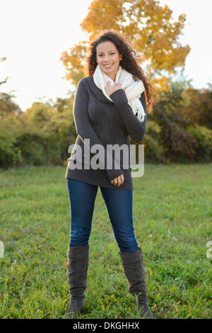Smiling curly-haired young woman standing on wall outdoors talking on ...