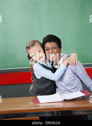 Schoolgirl Hugging Female Teacher At Desk Stock Photo - Alamy