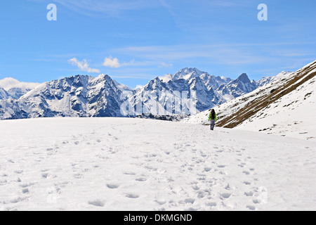 Alpinist hiking uphill on snowy slope in scenic high mountain landscape ...