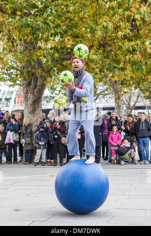 Street Performer juggler on blue ball juggles balls with help from ...