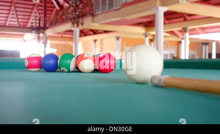 A pool table with a cue and no balls under the umbrella of outdoor cafe ...