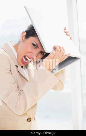 irritated woman screaming while holding laptop on yellow background ...