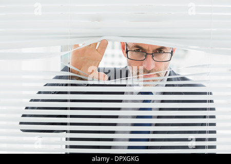 Close-up of a businessman peeking through blinds in office Stock Photo ...