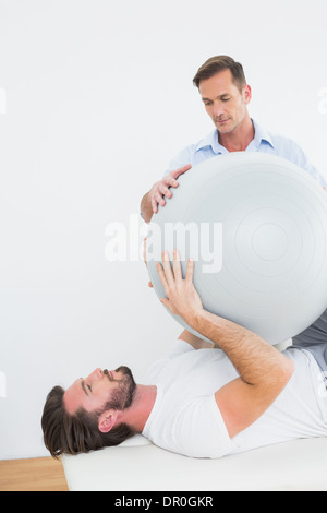 Physical therapist assisting man with yoga ball Stock Photo - Alamy
