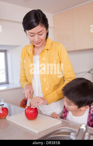 Son watching mother cut apple Stock Photo - Alamy