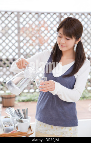 Young woman pouring water into glass on blue background Stock Photo - Alamy
