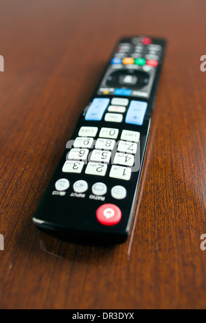 Remote control on wooden table and TV screen in room, selective focus ...