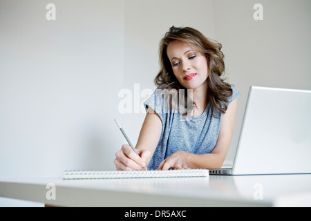 Woman taking notes while using laptop in the kitchen Stock Photo - Alamy