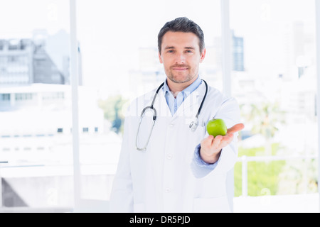 Portrait of a smiling male doctor holding an apple at a medical office ...