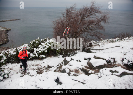 A runner makes his way up a snowy rocky path from the coast line of ...