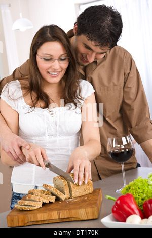 Happy couple cut bread in modern kitchen together and drink red wine ...