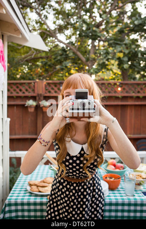 Young woman photographing through instant camera in front of shopping ...