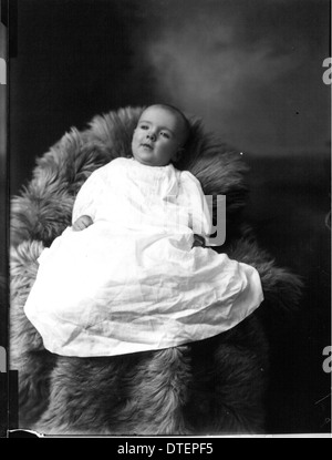 This 1912 portrait photograph shows a baby dressed in a long gown ...