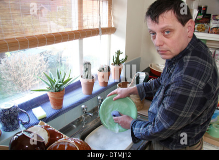 Man washing up pots with little enthusiam at a kitchen sink at home ...