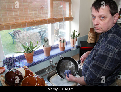 Man washing up pots with little enthusiasm at a kitchen sink at home ...