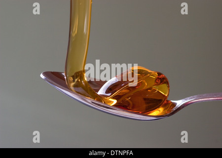 Golden syrup being poured onto silver spoon from above with a neutral ...