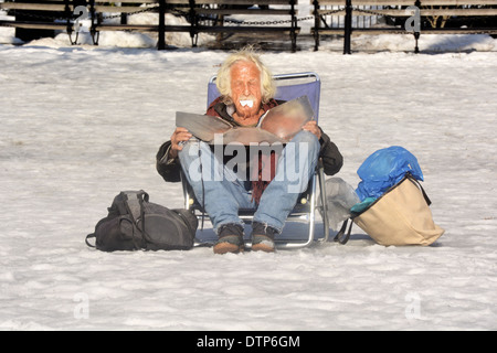 A man is snow tanning with a sun reflector on a lawn chair in ...