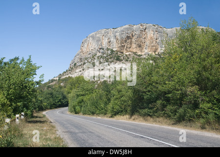 Empty road winding among rocks and lush green hills with pine trees ...