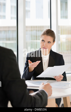 Female professional gesturing while discussing with colleague through ...