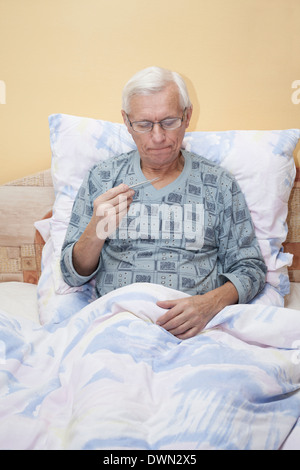 Ill senior man checking temperature with thermometer in bed Stock Photo ...