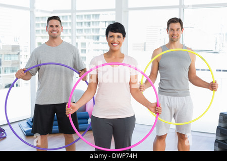 Portrait of fitness class holding hula hoops around waist in bright gym ...